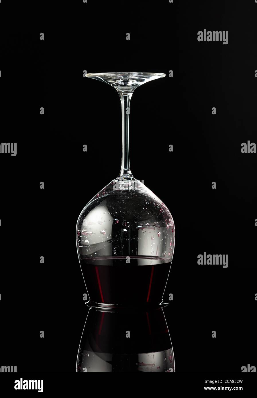 Inverted wine glass with red wine on a black reflective background ...