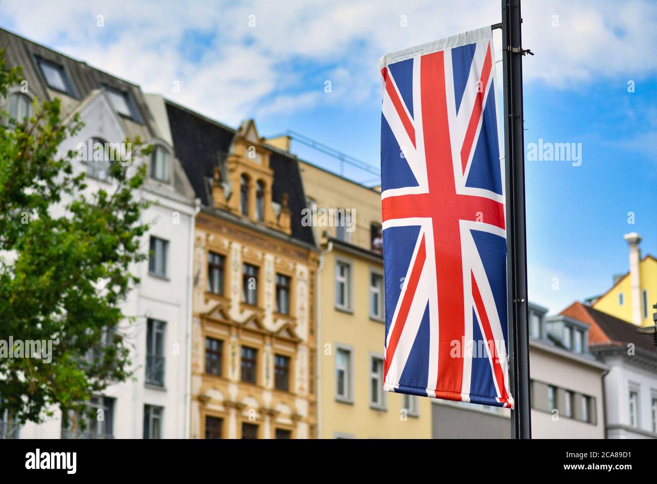 British Union Jack flag hanging on pole in front of blurry city street ...