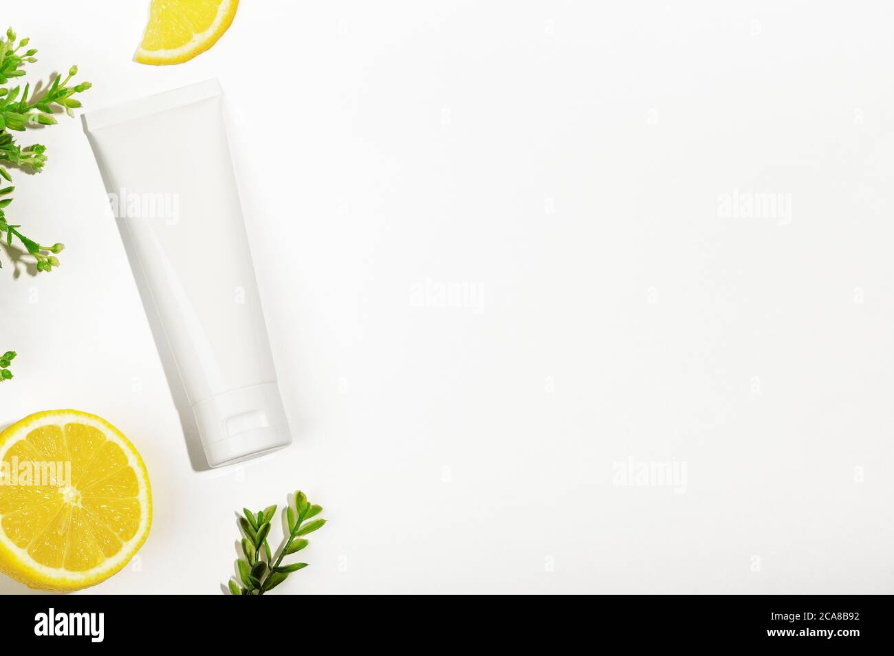 Top view of white unbranded tube with green plant and juicy lemon ...