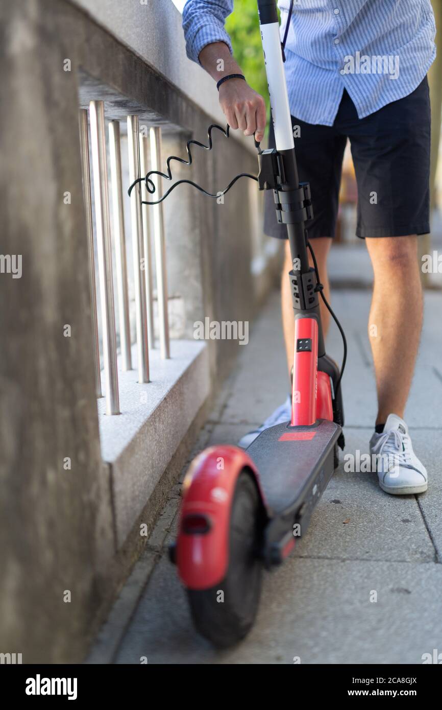 Male user safely parking electric scooter and locking it to a fence ...