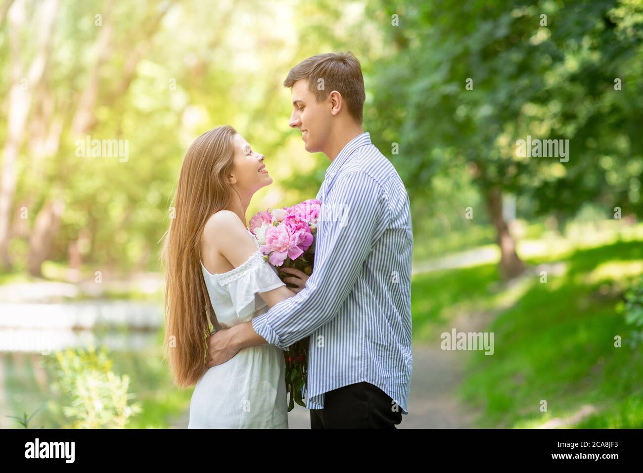 Lovely girl with bouquet of peonies hugging her boyfriend on romantic date at park Stock Photo ...