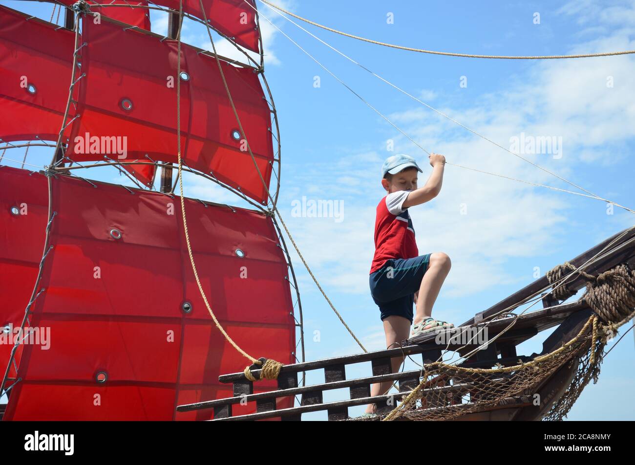 boy looks into the distance on an old ship with red sails. boy under ...