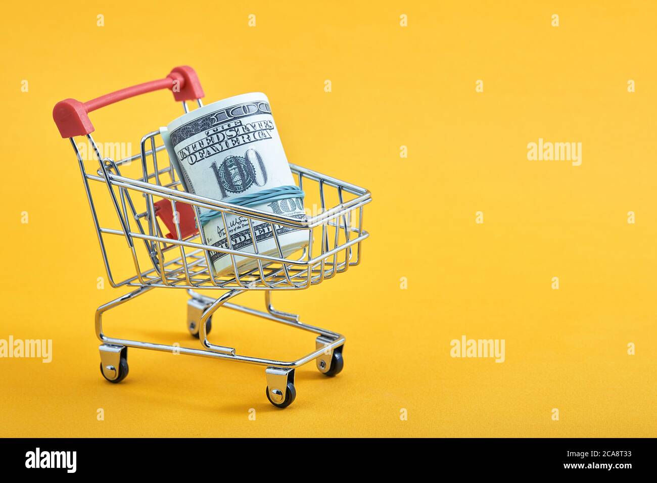 Mini shopping cart with 100 dollar banknotes inside on yellow ...
