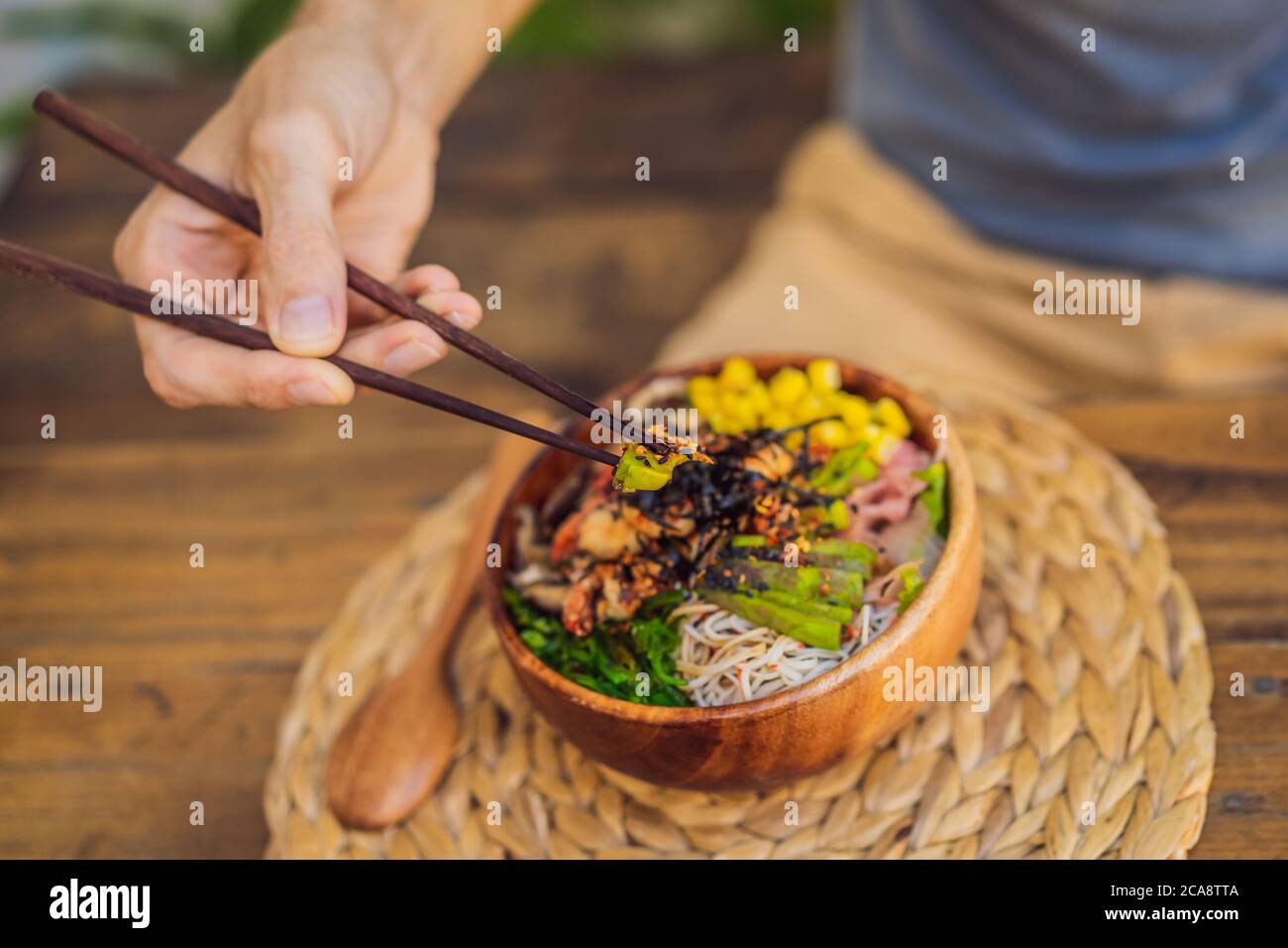 Man eating Poke bowl with shrimp, corn, avocado, ginger and mushrooms ...