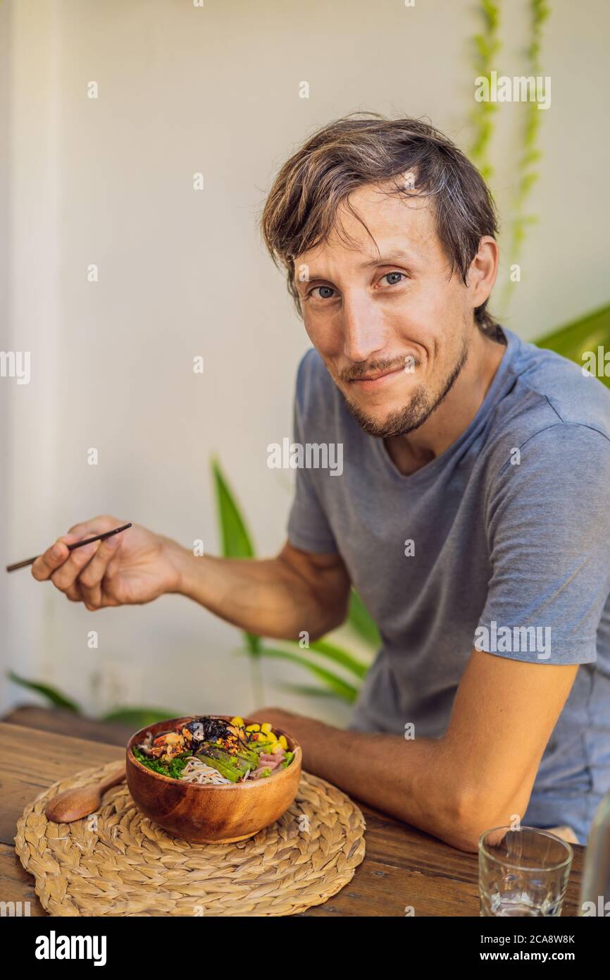 Man eating Poke bowl with shrimp, corn, avocado, ginger and mushrooms ...