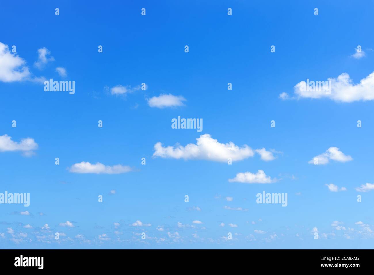 Sparse small white fluffy clouds float slowly high in the bright blue ...