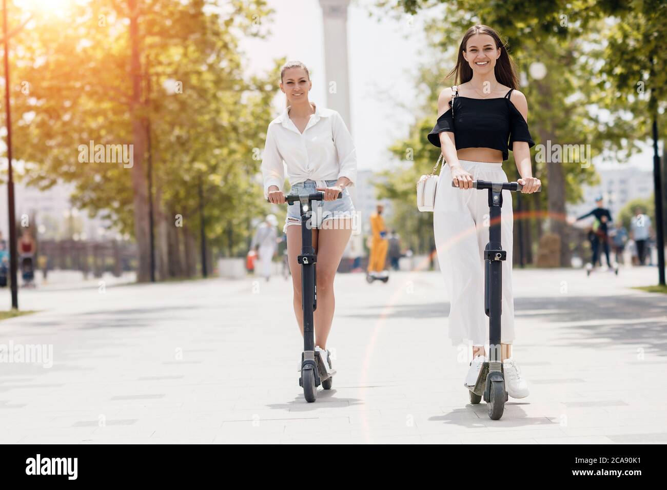Two women friends riding electric scooters in park Stock Photo - Alamy