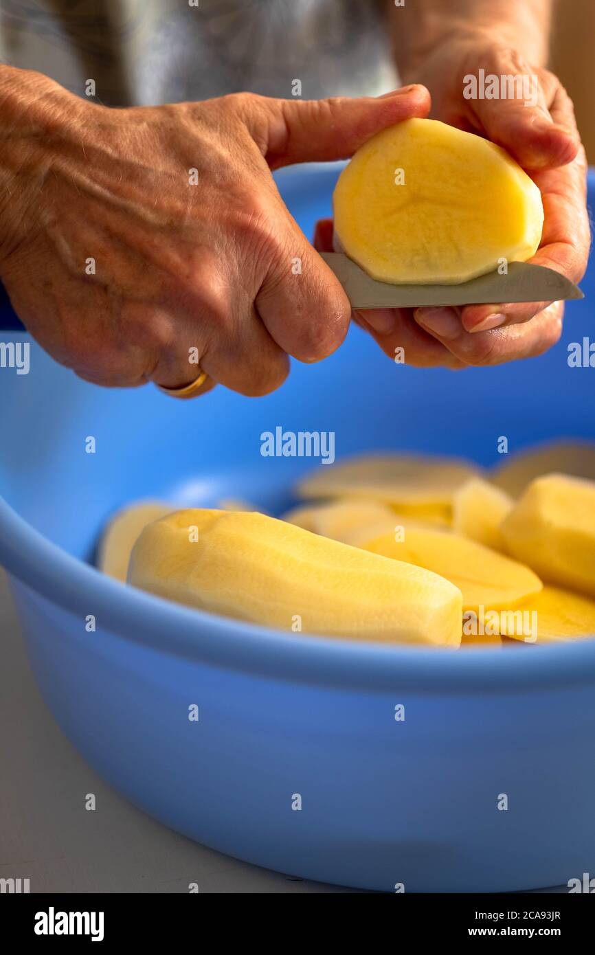 Woman sliced potatoes in round shape with knife in a blue bowl. Fresh ...
