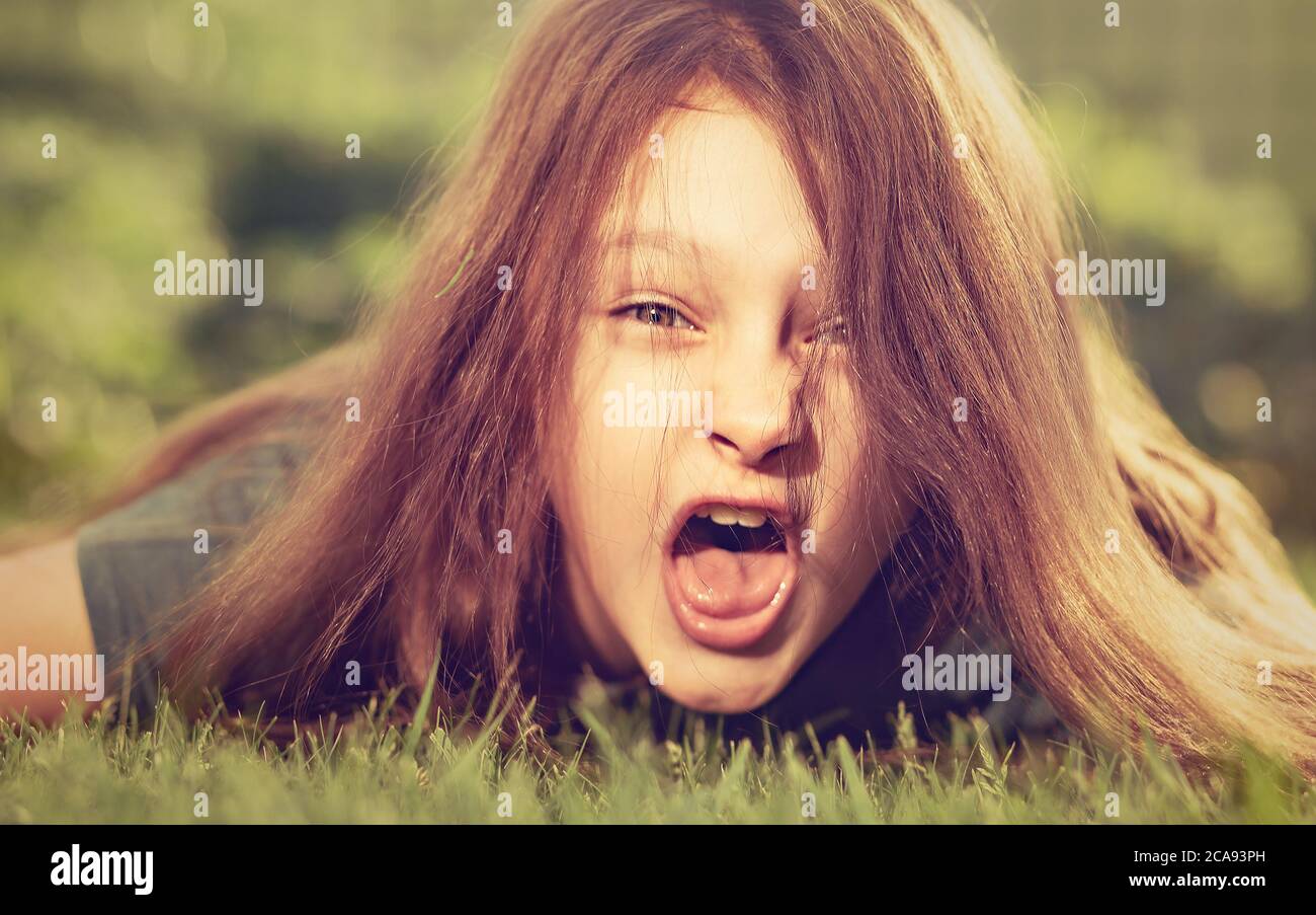 Crazy angry kid girl shouting with opened mouth and mad hair lying on ...