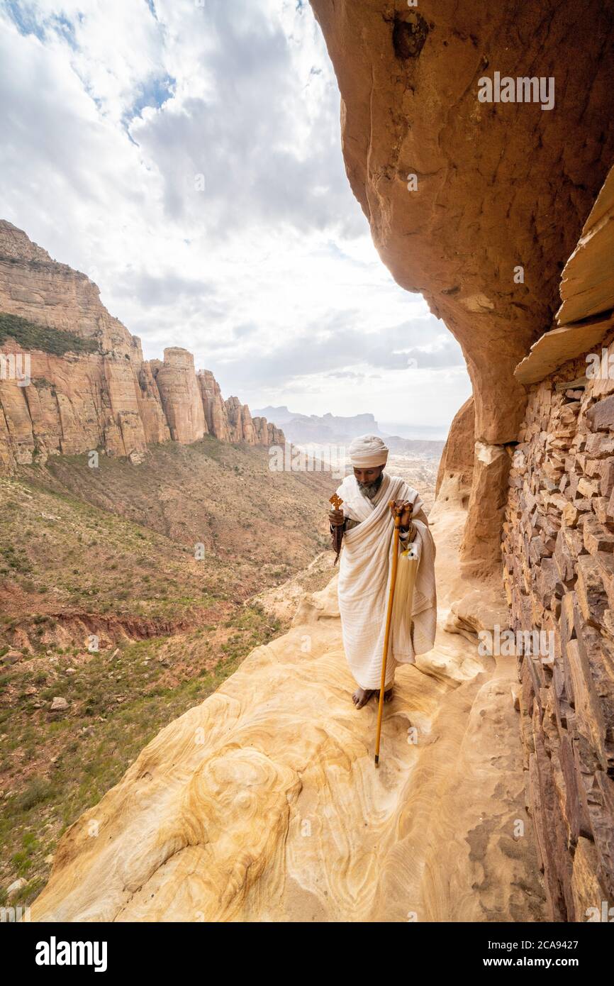 Priest holding the hand cross on rocks outside Abuna Yemata Guh church, Gheralta Mountains ...