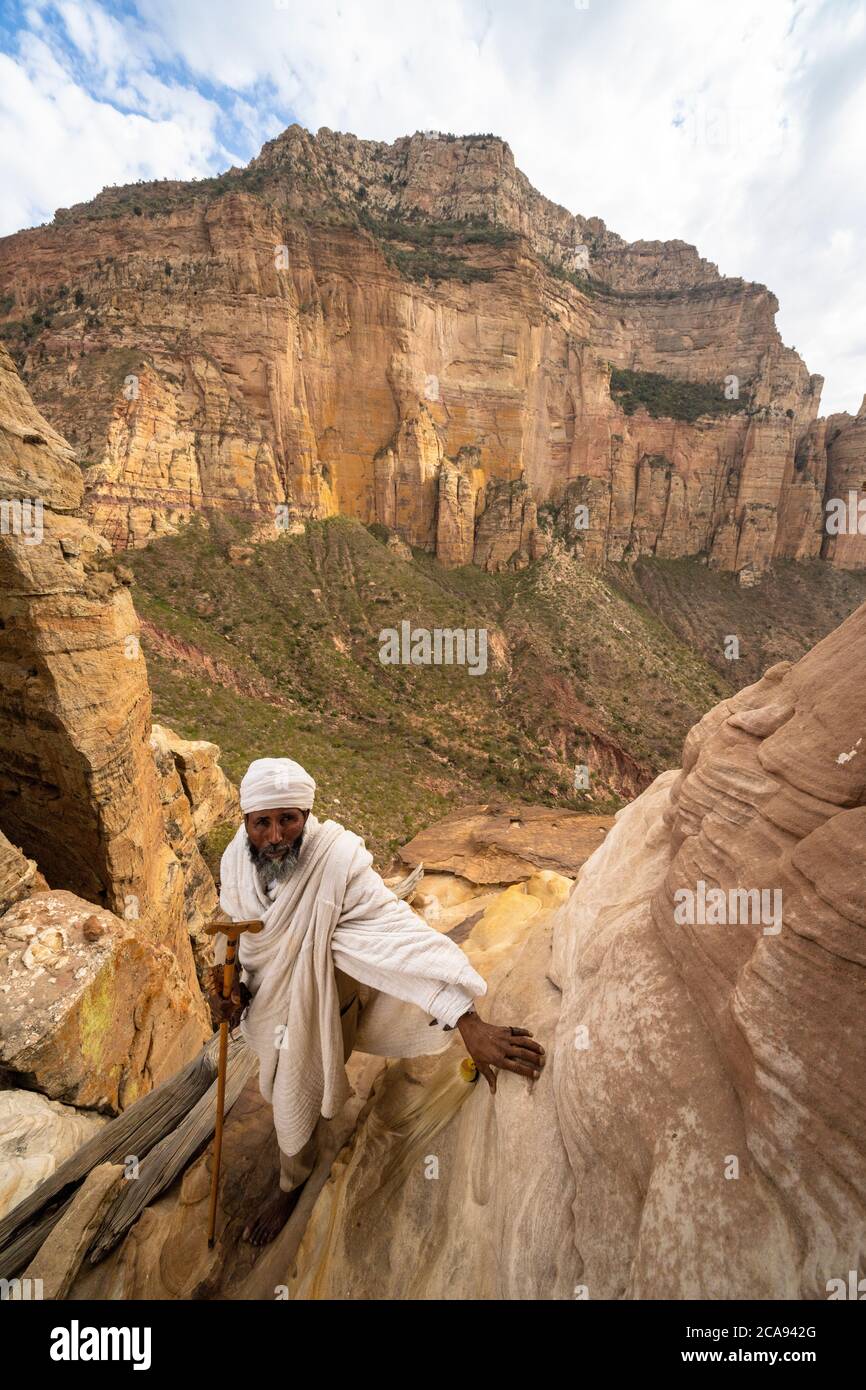 Ethiopian priest leaning on steep rocks leading to Abuna Yemata Guh church, Gheralta Mountains ...