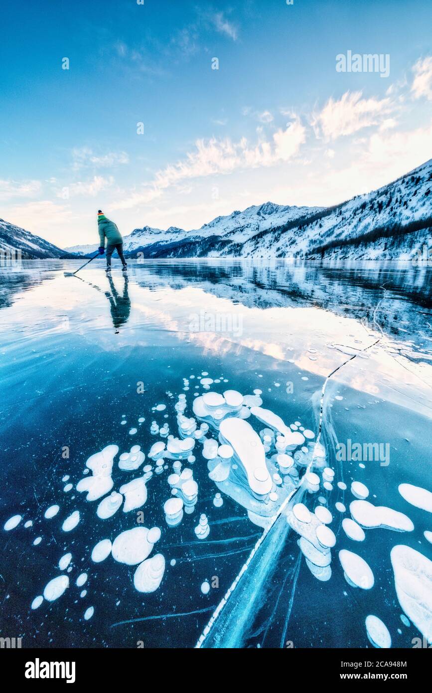 Man playing ice hockey on frozen Lake Sils covered of bubbles, Engadine ...