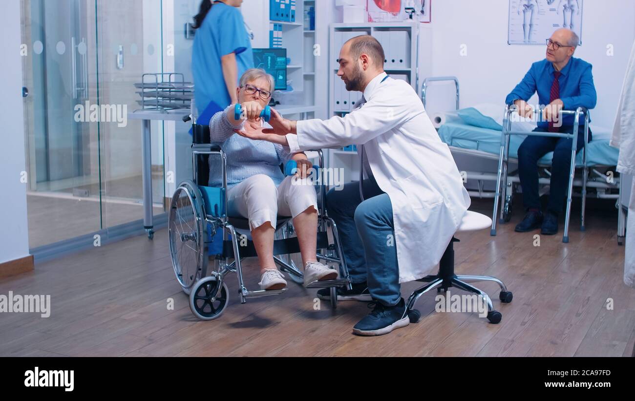 Doctor helping old disabled woman in wheelchair to regain muscle ...