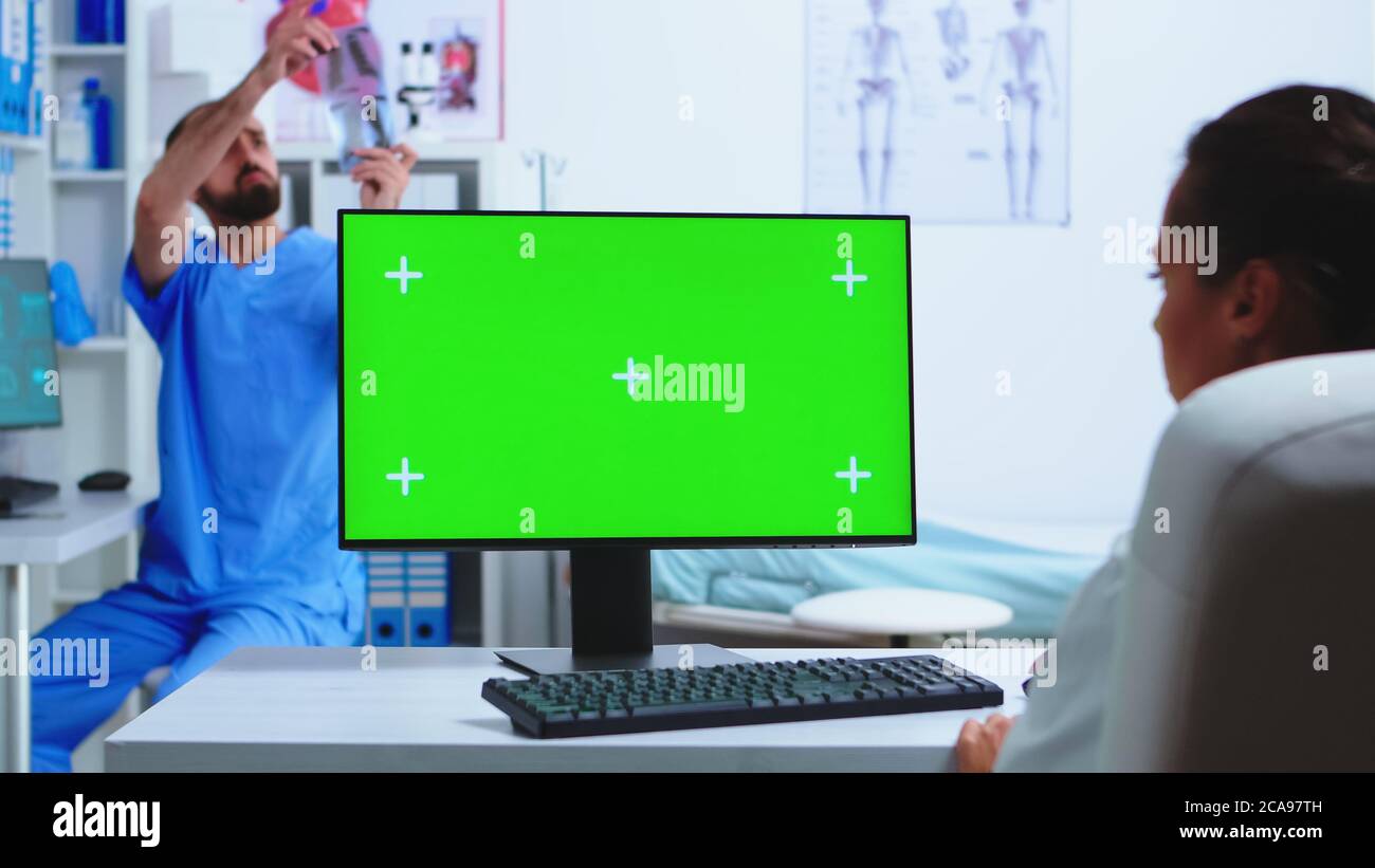 Doctor working on computer with green screen in hospital and assistant ...