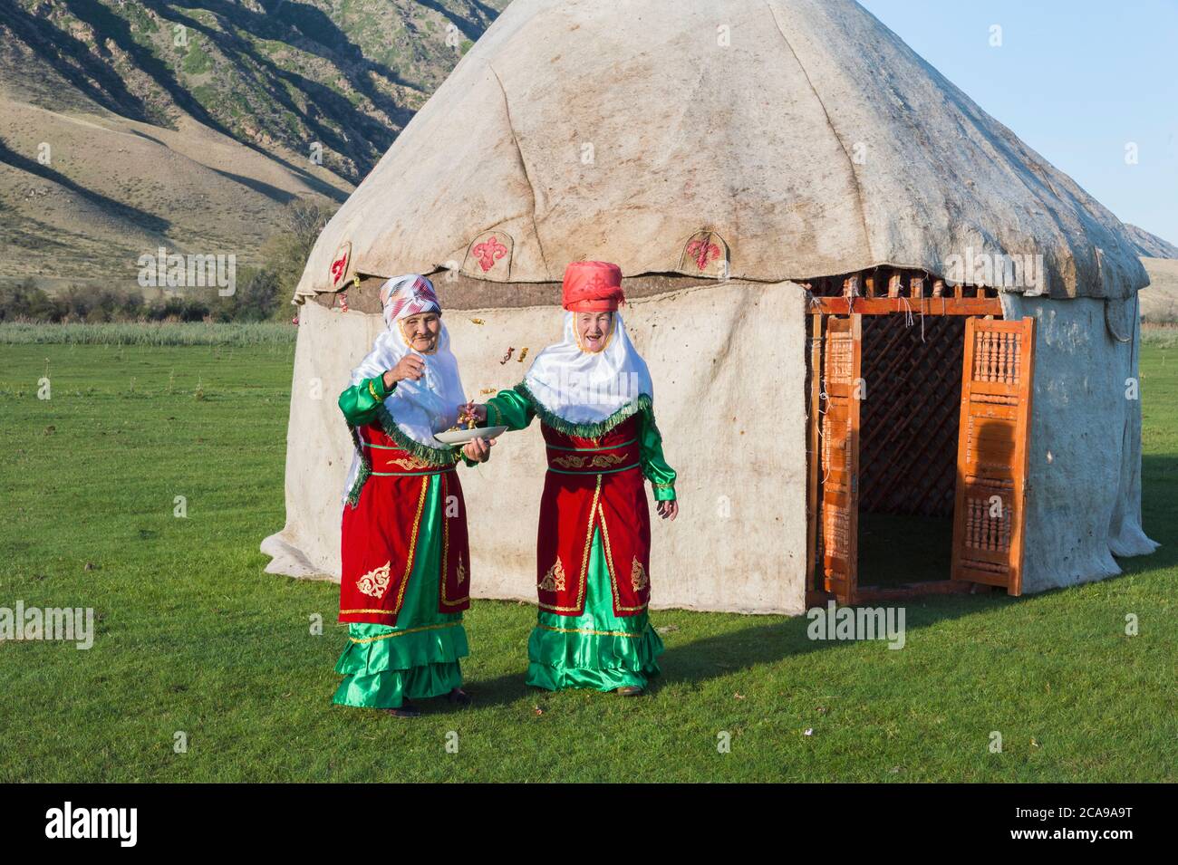 Two Kazakh women in traditional clothes in front of a yurt welcoming ...