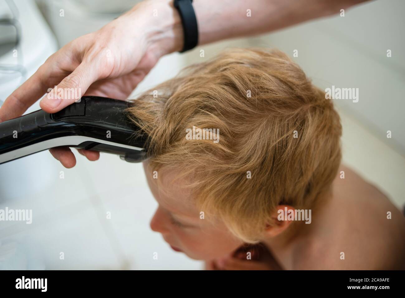 Father making haircut for son at home with haircut machine in bathroom ...