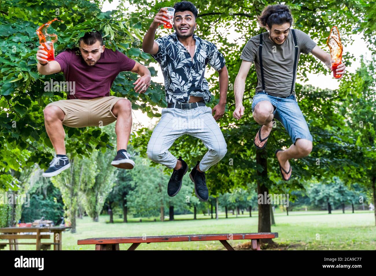 group of millennial people having fun jumping while drinking colorful ...