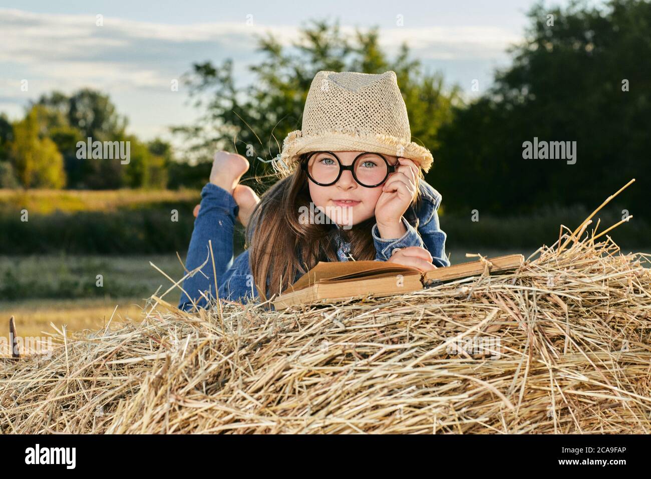 Reading girl sits over the haystack roll on field in countryside. High ...
