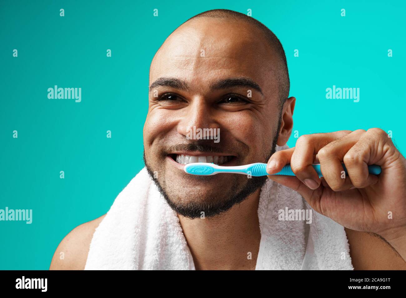 Cheerful dark-skinned male brushing his teeth against turquoise ...