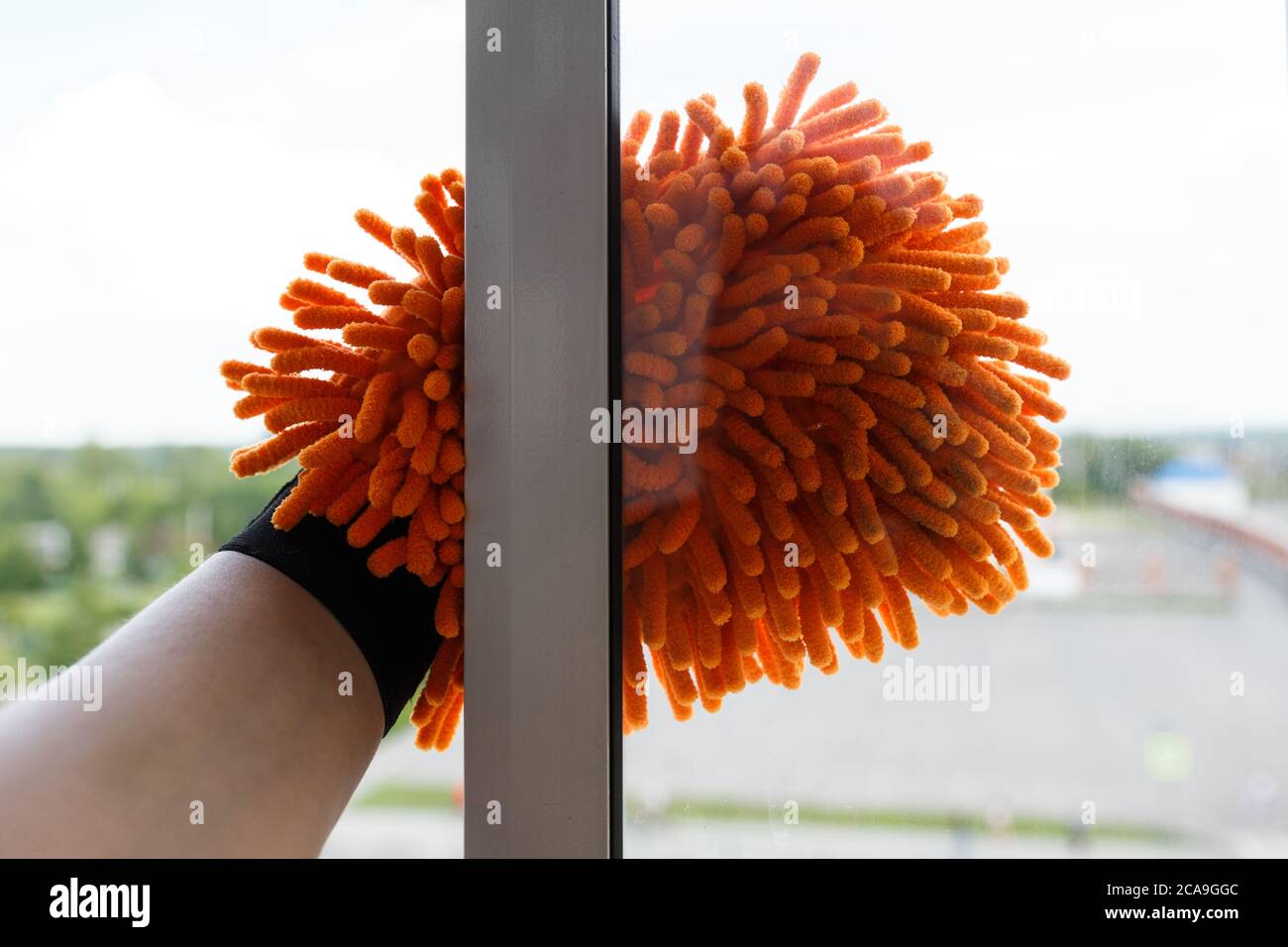 A man's hand with an orange window-cleaning mitt washes the window ...