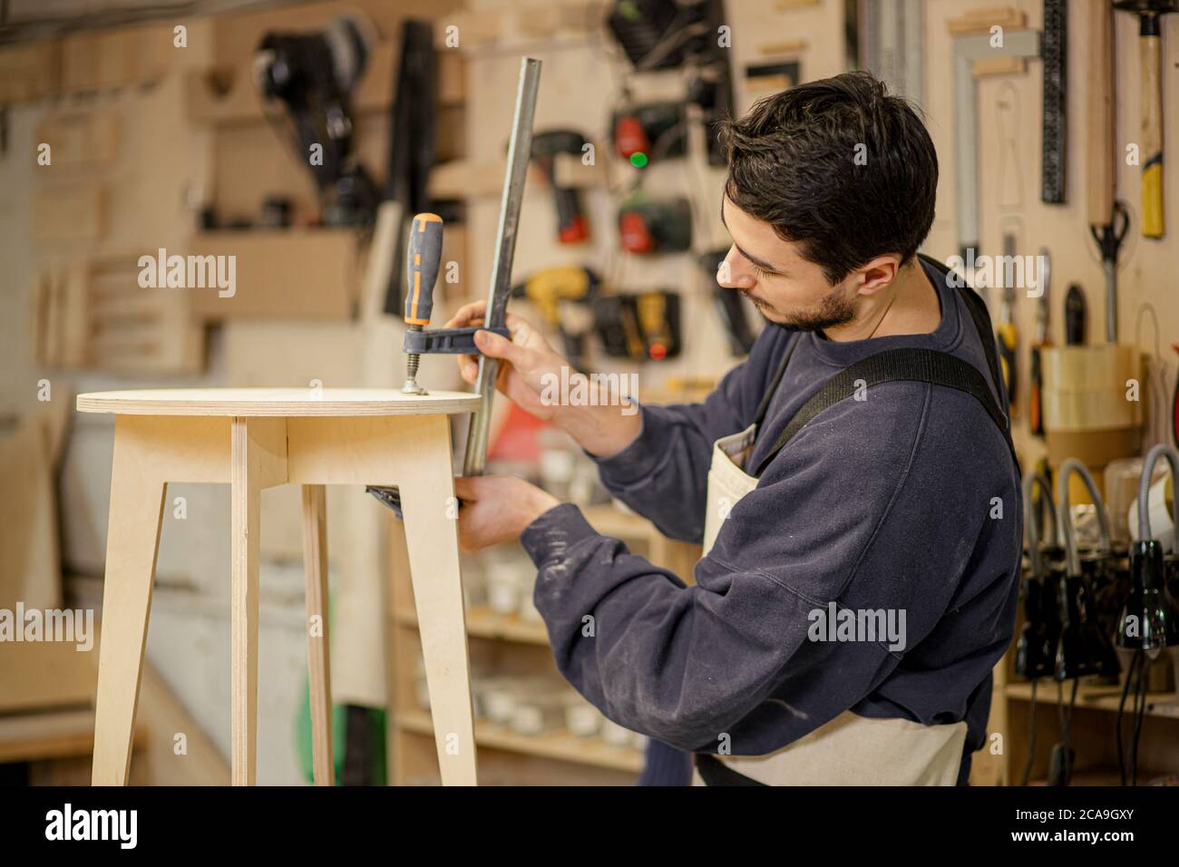 portrait of hardworking carpenter man in uniform making wooden chair on ...