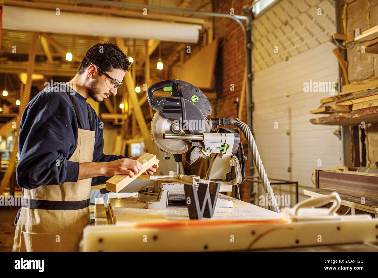 confident young carpenter work with mitre saw in factory, stand ...