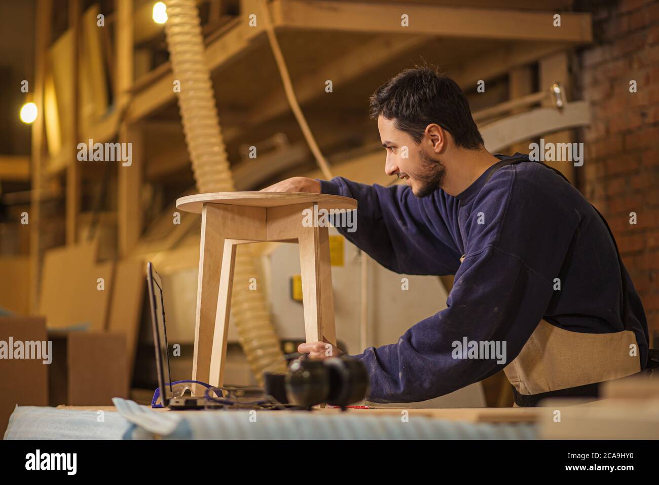 young caucasian carpenter measuring chair height in workshop, preparing ...