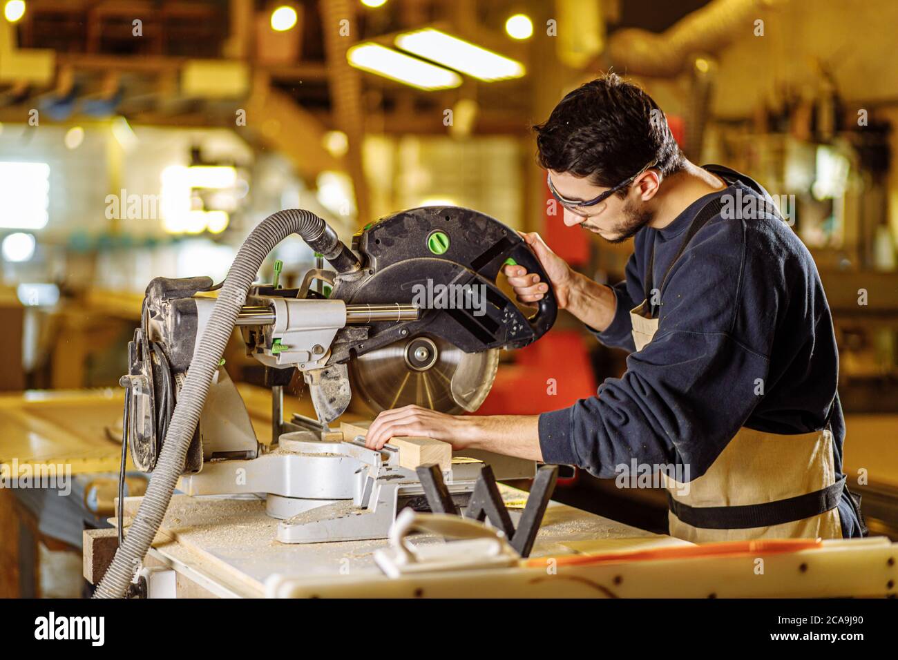 confident young carpenter work with mitre saw in factory, stand ...