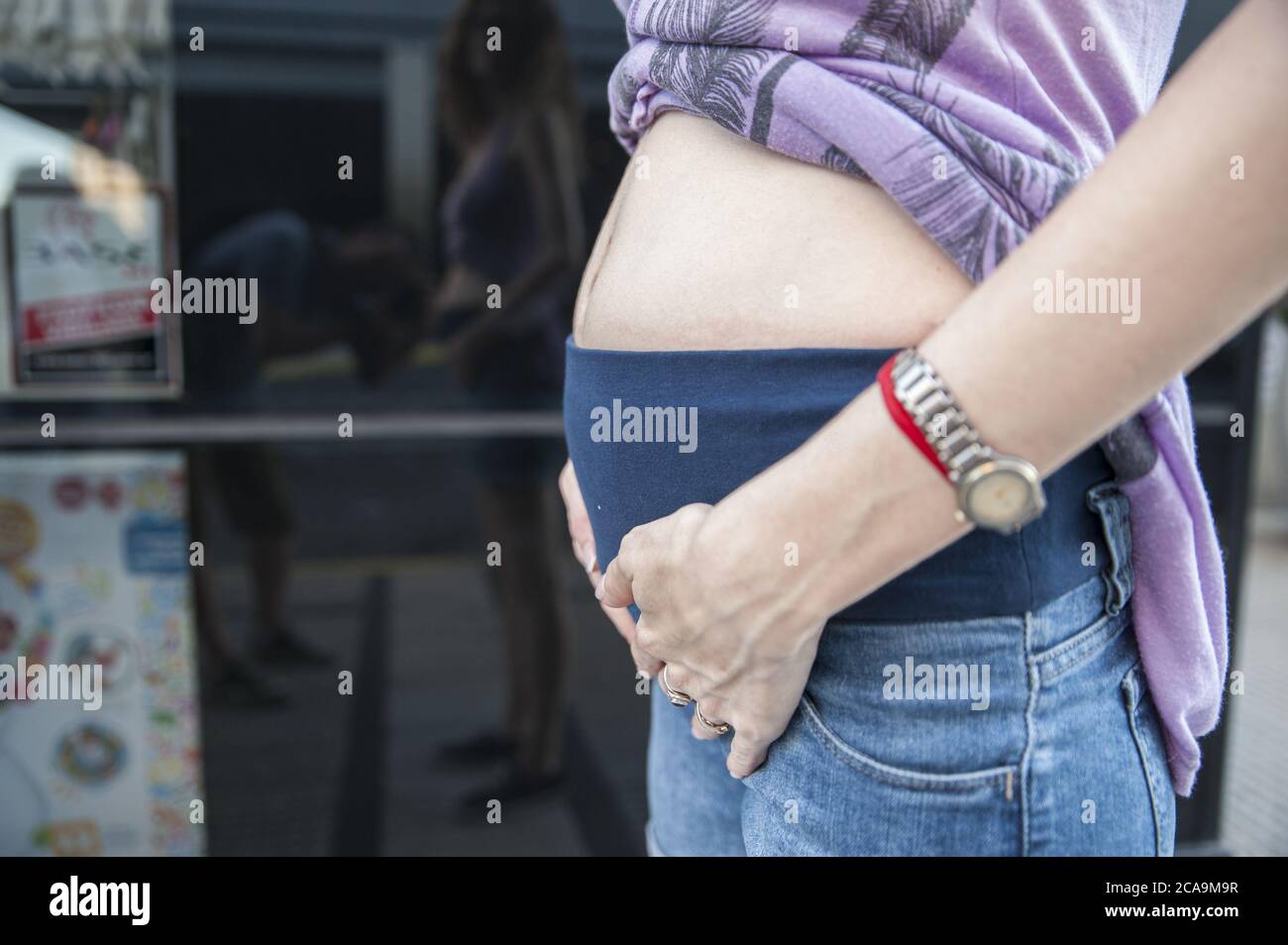 Pregnant female with her belly looks at her reflection on a window ...
