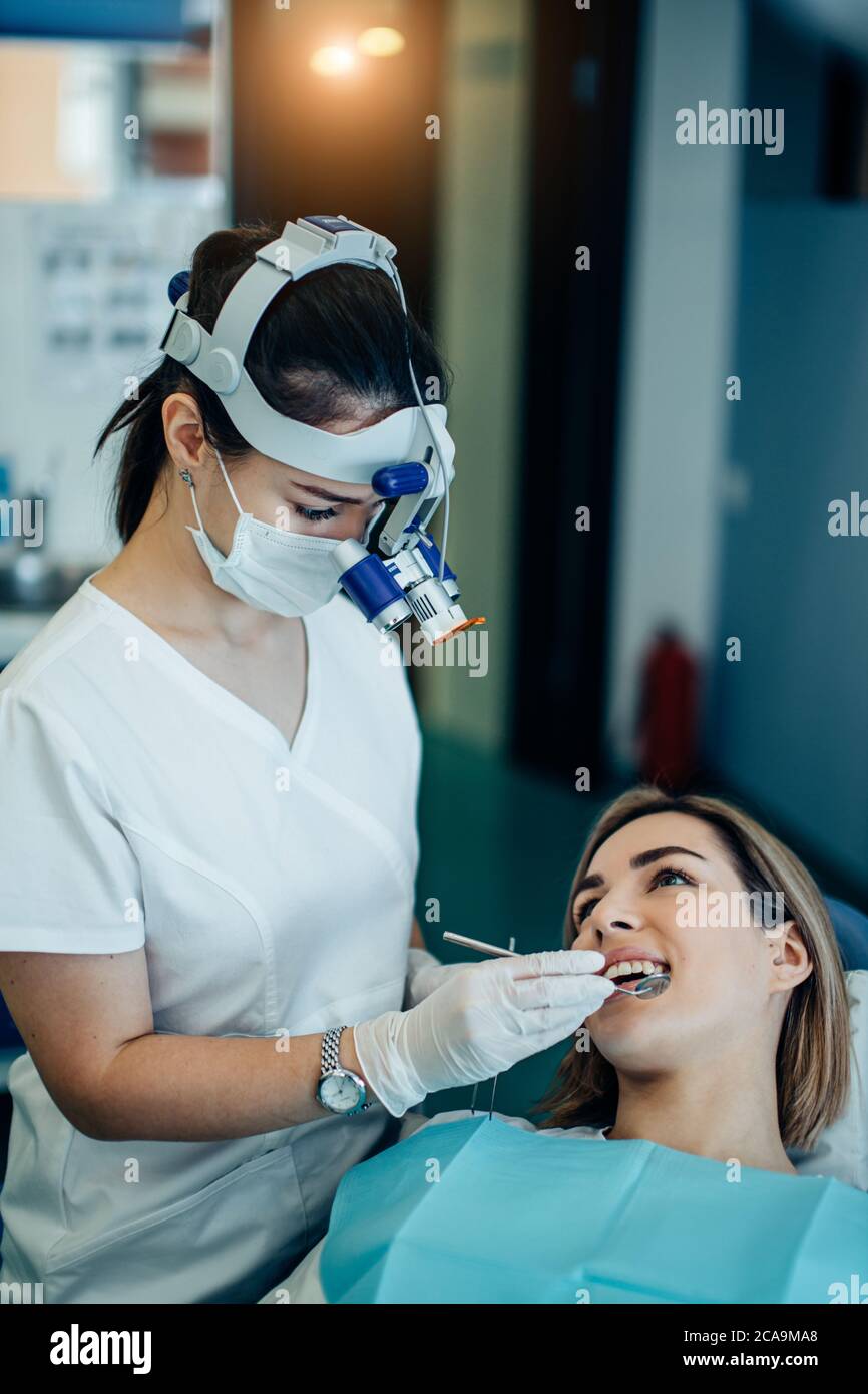 young dentist doctor in white uniform and special forehead lamp examine ...