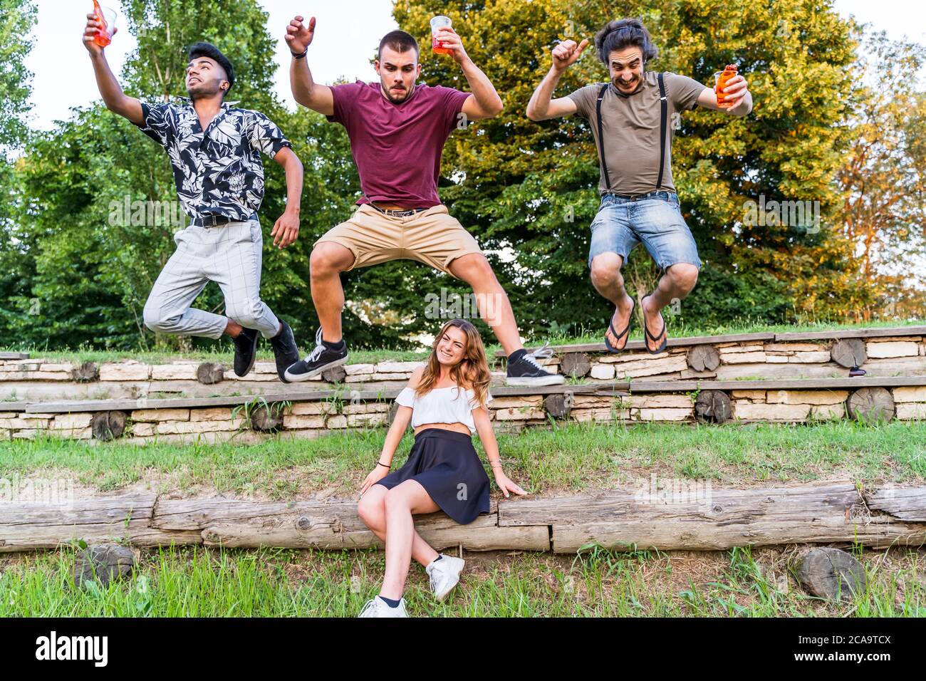 group of millennial people having fun jumping while drinking colorful ...