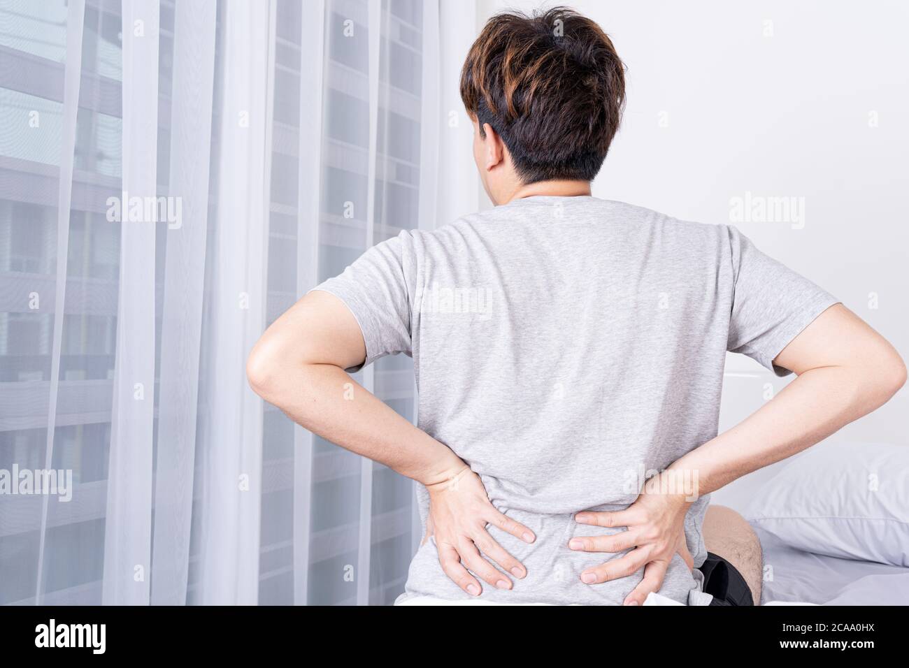 Young man suffering back pain from uncomfortable bed. Healthcare ...