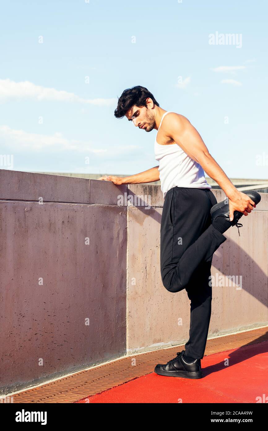 vertical photo of a handsome sportsman stretching his leg muscles on a ...
