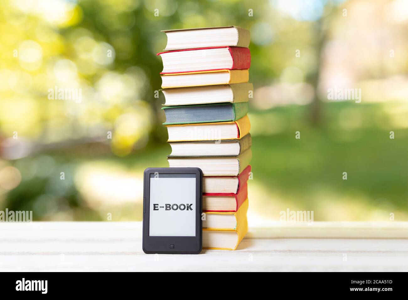 Reading. E-book reader and a stack of books. The park is blurred in the ...