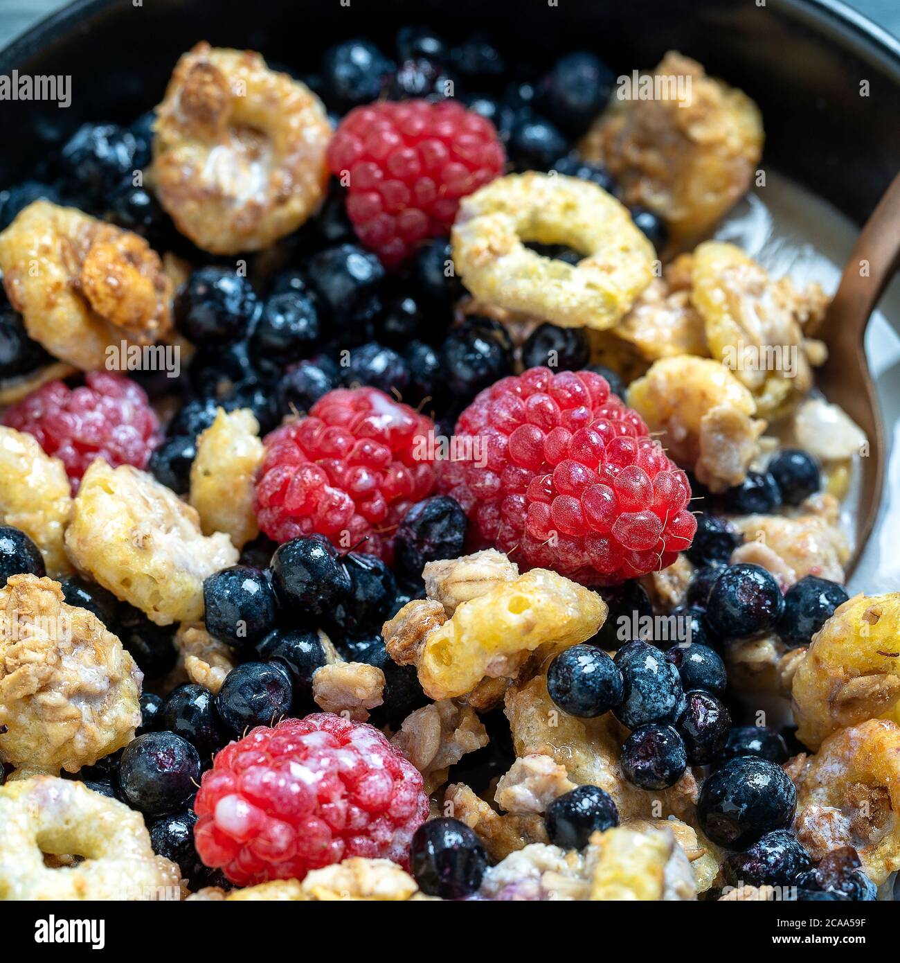 Muesli with raspberries, blueberries and flakes in a black bowl, close ...