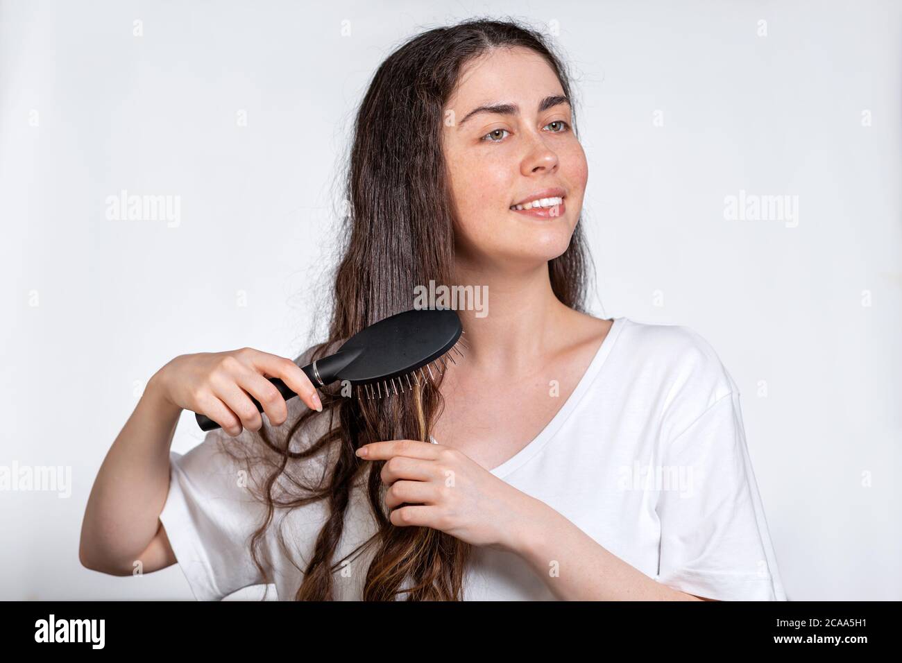 Pretty smiling brunette woman combs her hair. White background. Hair ...