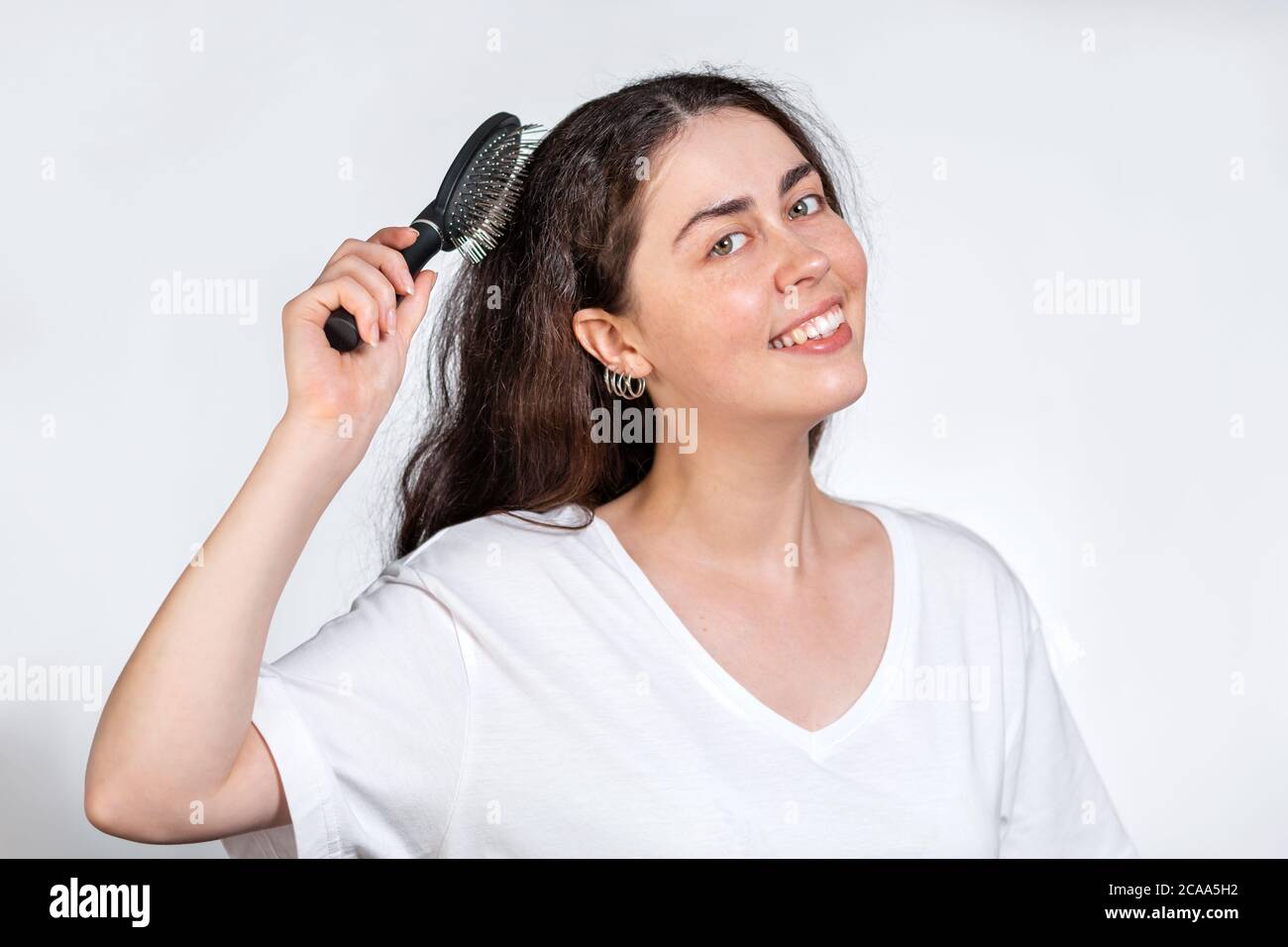 A pretty brunette woman smiles and combs her hair. White background ...