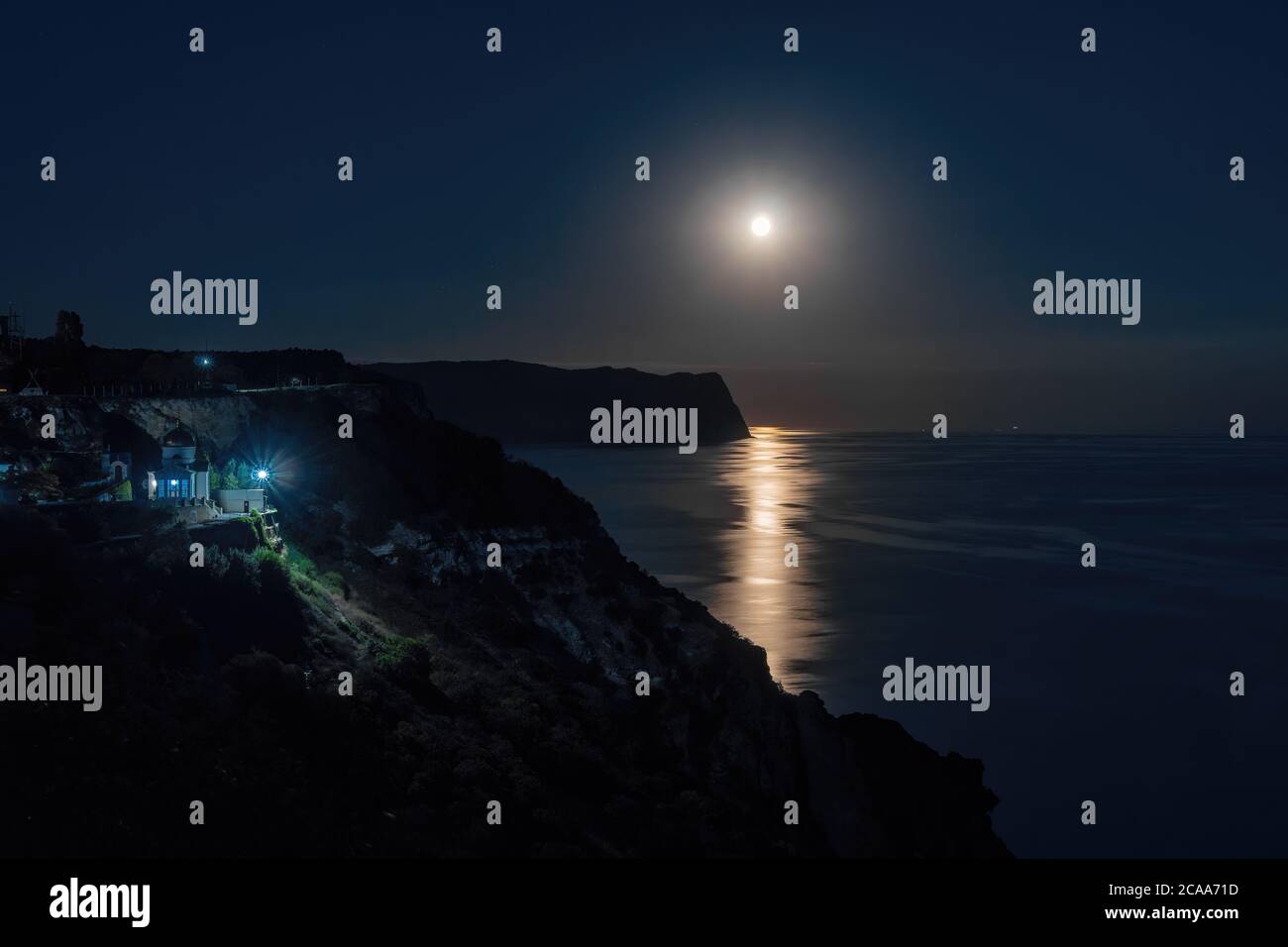 The full moon rises in a starry night sky over the sea and rocky cliffs ...