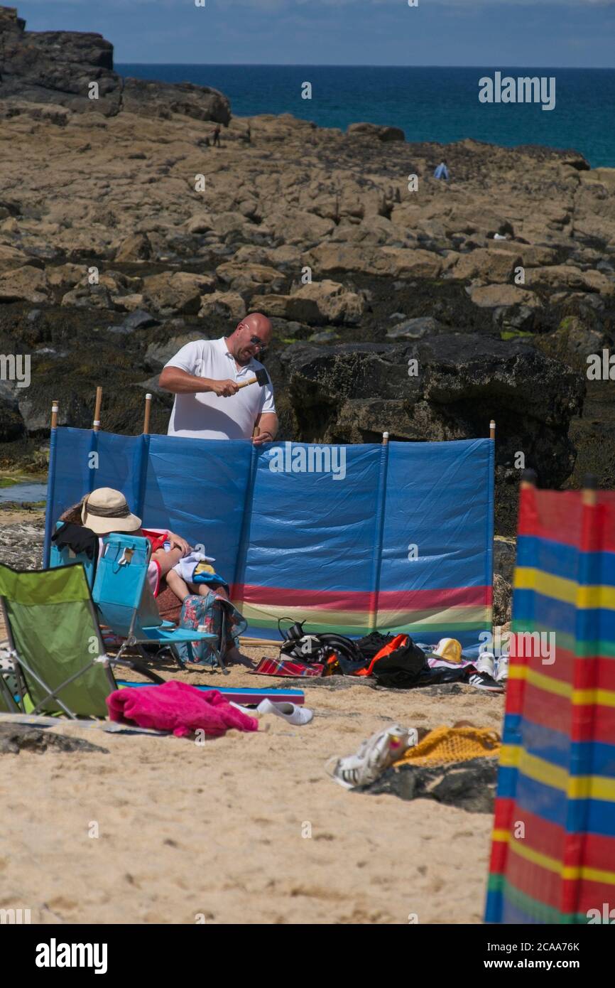 Man erecting wind break on beach. Standing with mallett over posts Blue ...