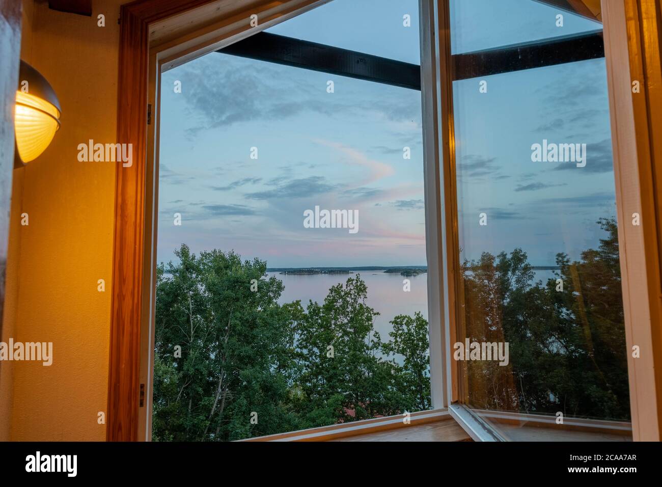 Beautiful summer sundown view from open window. Top of green trees on ...
