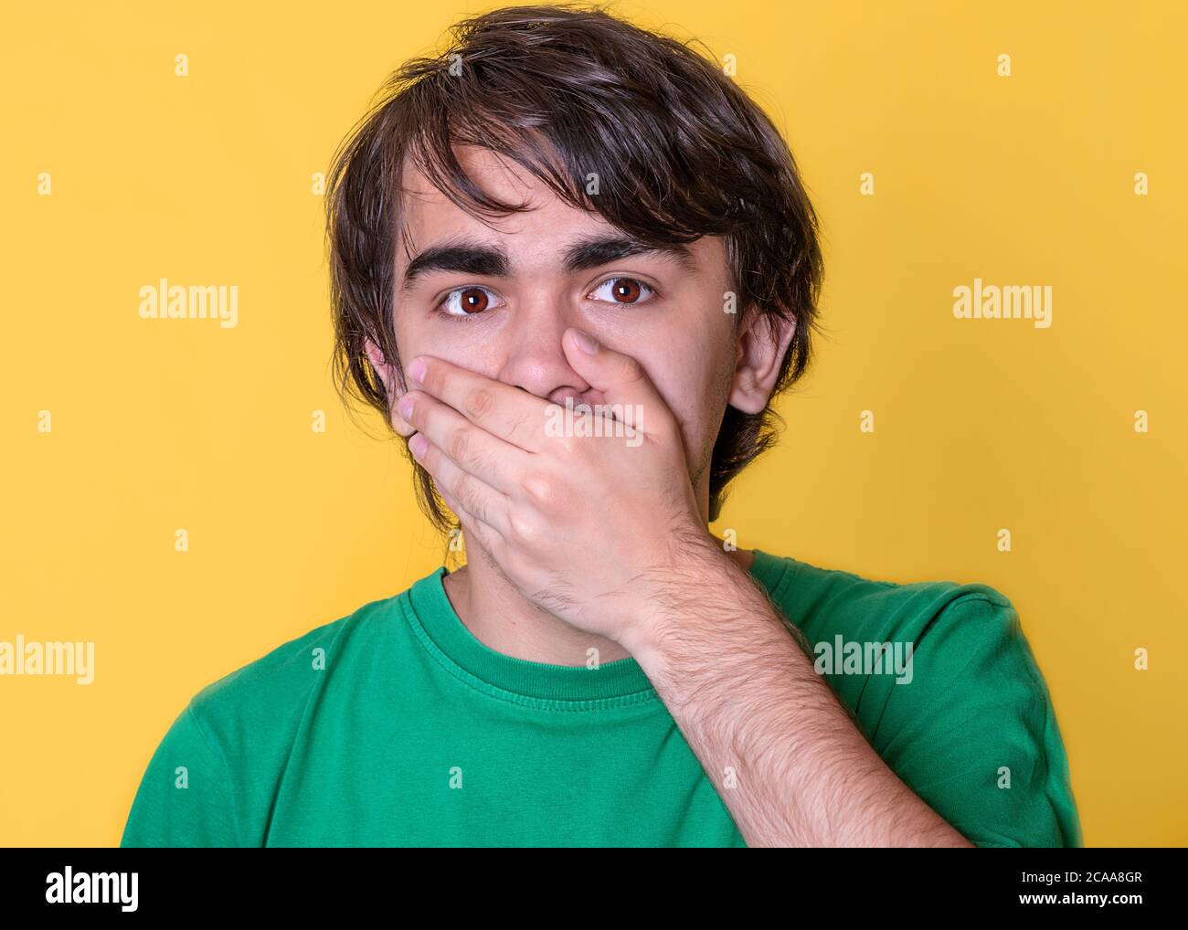 the young man putting his hand over his mouth on yellow background ...