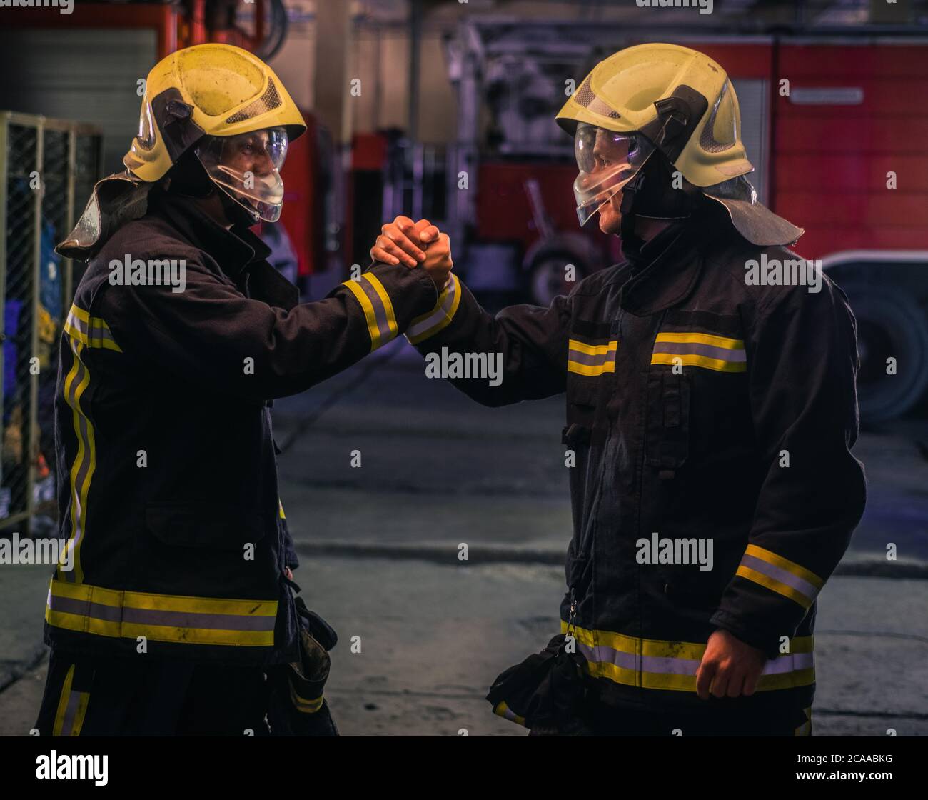 Portrait of two young firemen in uniform standing inside the fire ...
