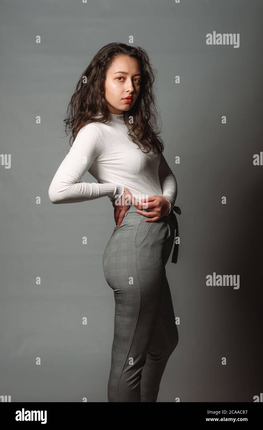 Portrait of a beautiful female model posing in white pullover over grey ...