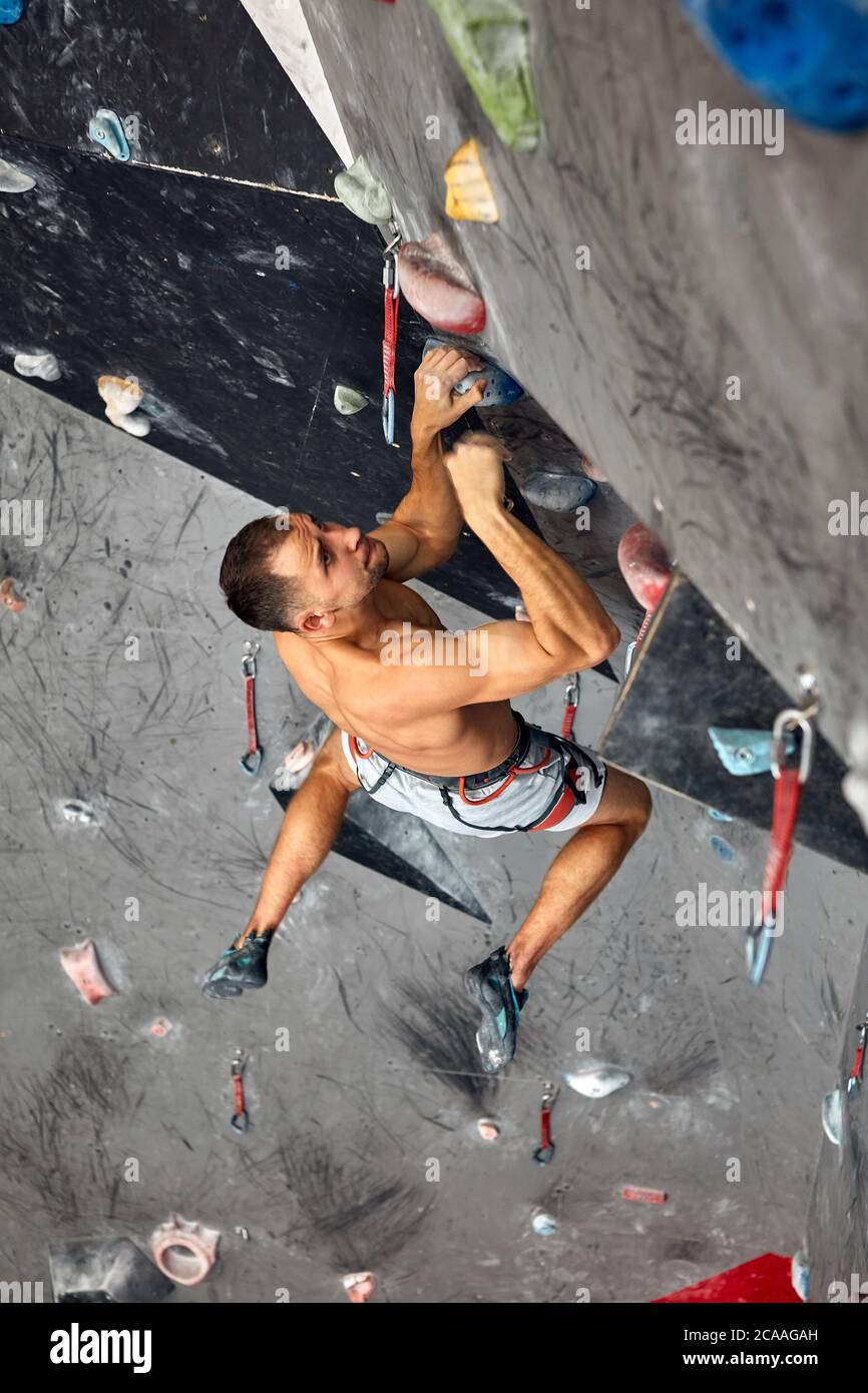 Athletic shirtless man hanging on hands at an indoor climbing centre ...