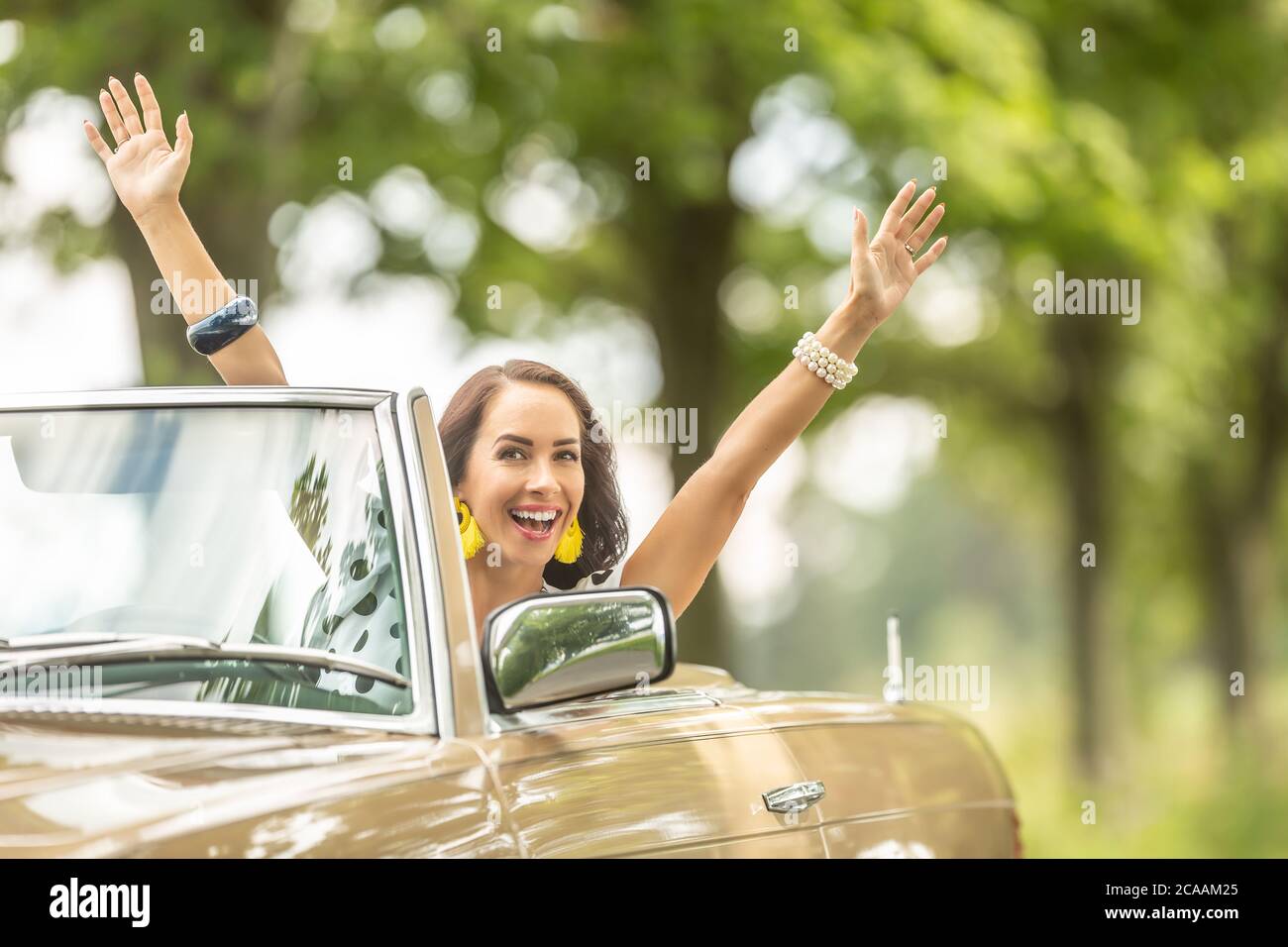 Beautiful woman in a beige convertible with arms above her smiling into ...