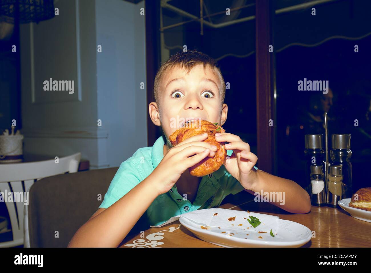 Adorable playful boy making face while biting delicious pie having meal ...