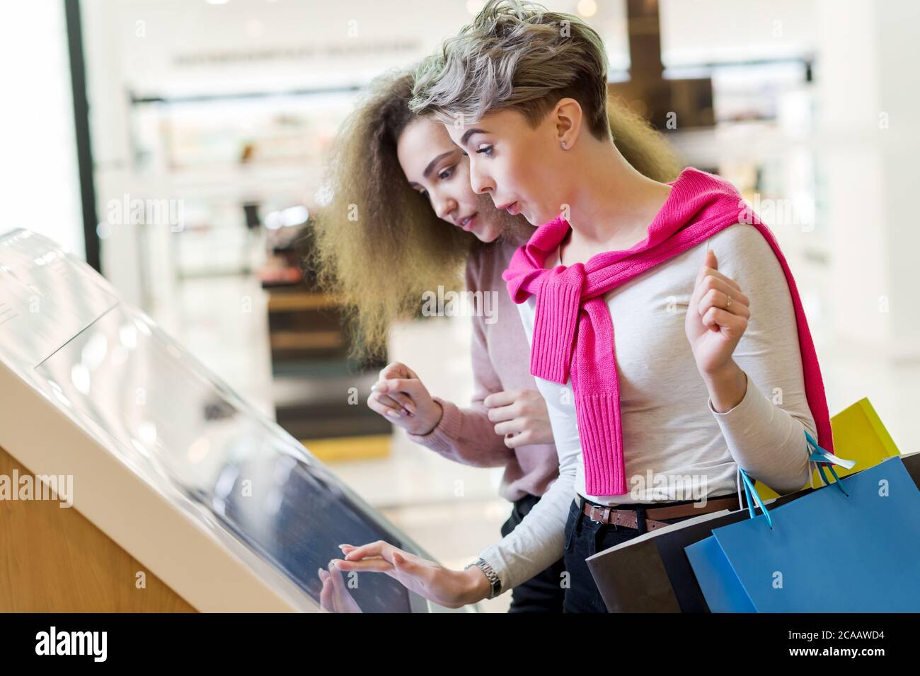 Two adult caucasian girlfriends use information kiosk at shopping ...