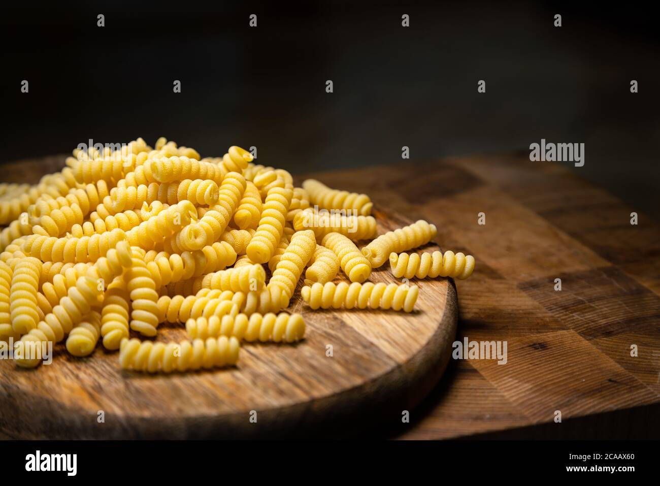 Uncooked curly pasta on wooden table background. Stack of traditional ...