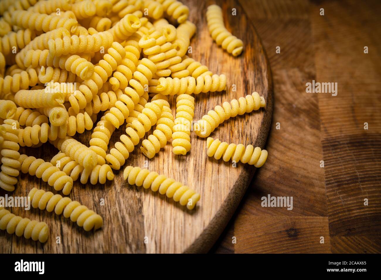 Uncooked curly pasta on wooden table background. Stack of traditional ...