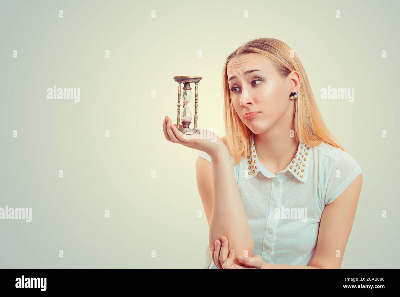 Blond woman making pity face expression and looking at hourglass in ...
